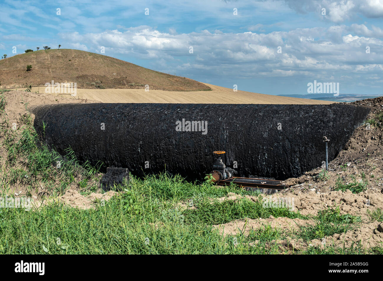 Black Oil pipeline goes out above the ground. Oil-stained pipe. Concept ...