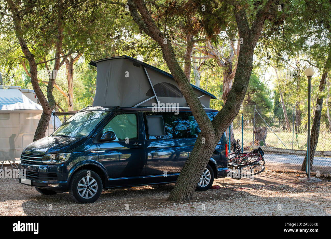 Dark blue camper caravan on camping. Morning sun. Motorhome on campsite ...
