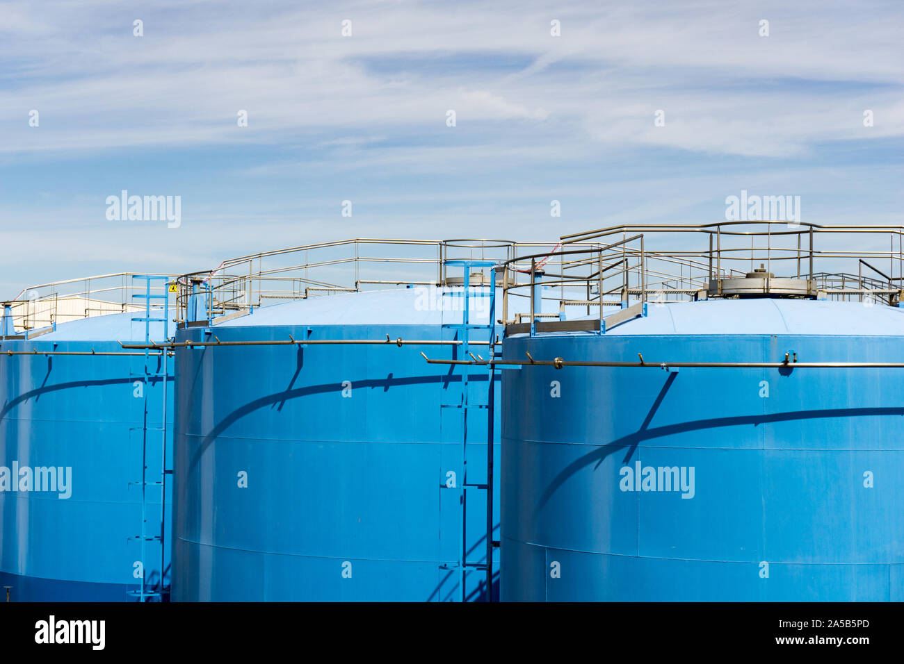 A horizontal view of many large blue indsutrial silos or storage tanks ...