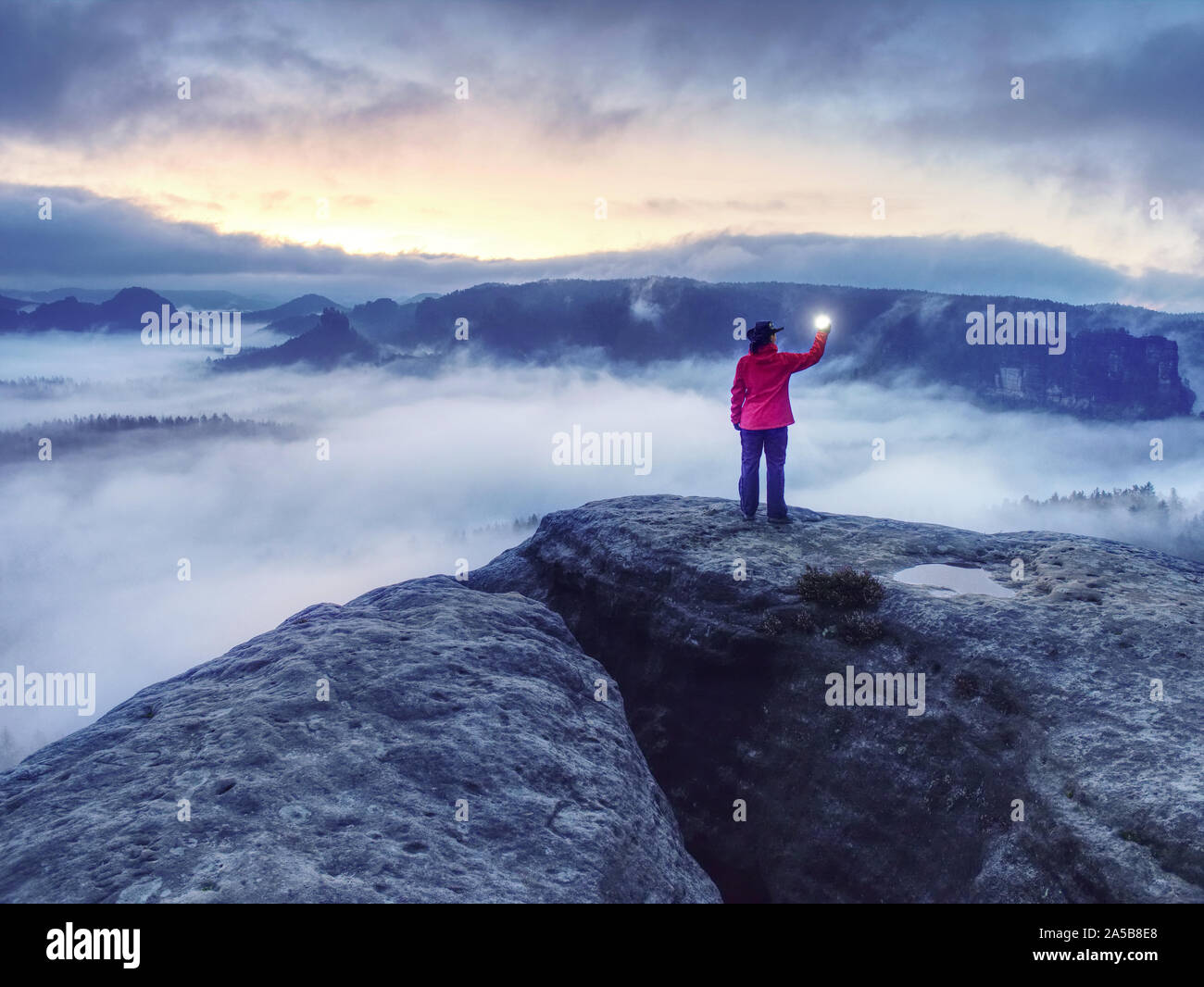 Tourist girl traveler stands on top of mountain holding strong light up ...
