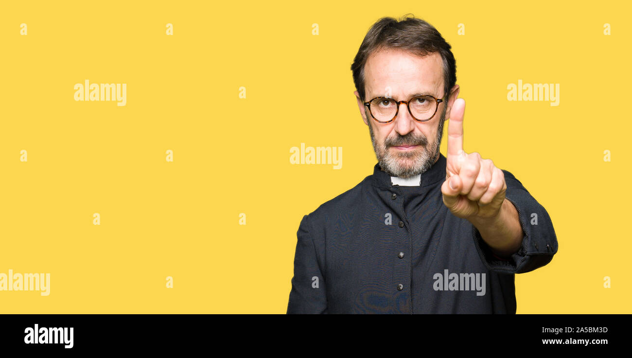 Middle age priest man wearing catholic robe Pointing with finger up and ...