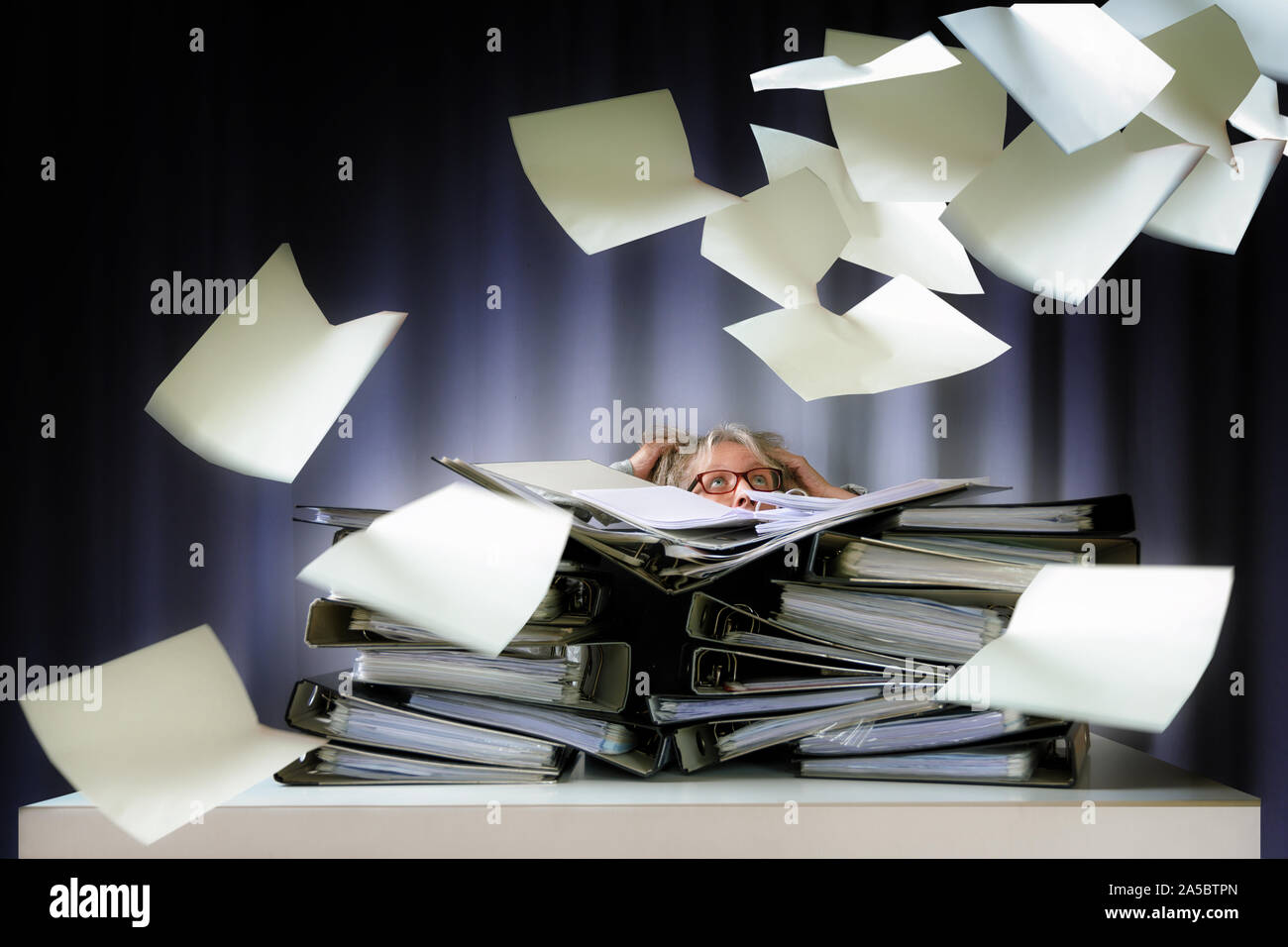 desperate woman sinks behind stacks of ring binders on an office desk ...