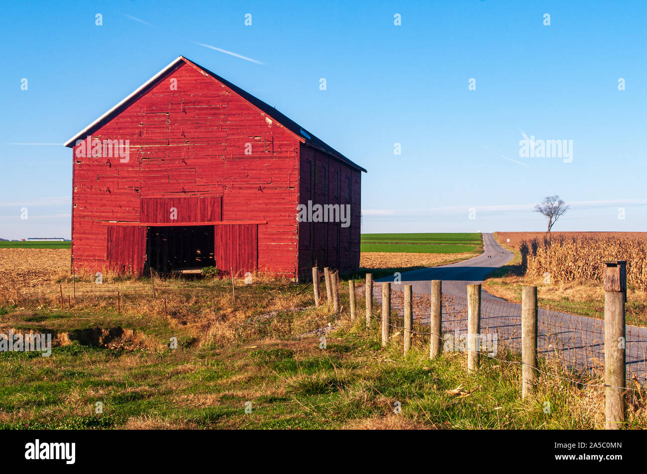 A simple red barn stands alongside a curve in a quiet country road in ...
