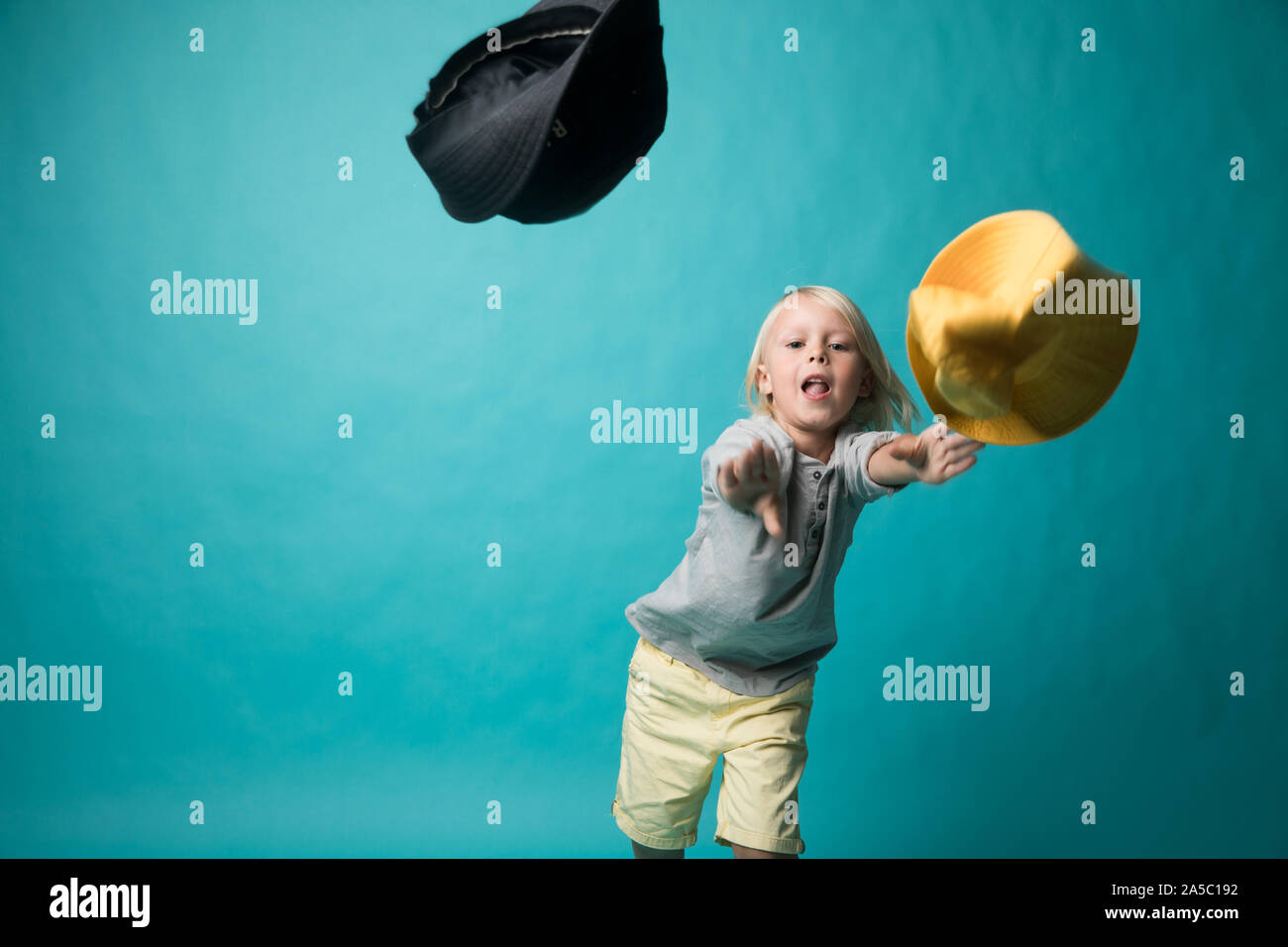 A boy on a blue background throws a yellow and black hat at the camera ...