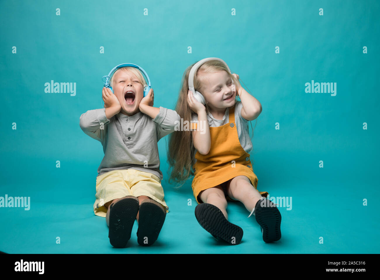 Very emotional children listen to music with headphones on a blue ...