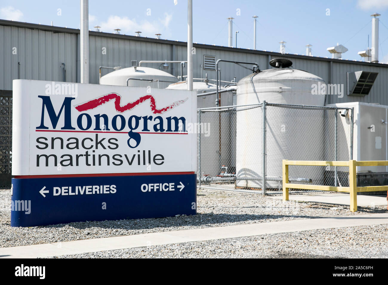A logo sign outside of a facility occupied by Monogram Snacks, a ...