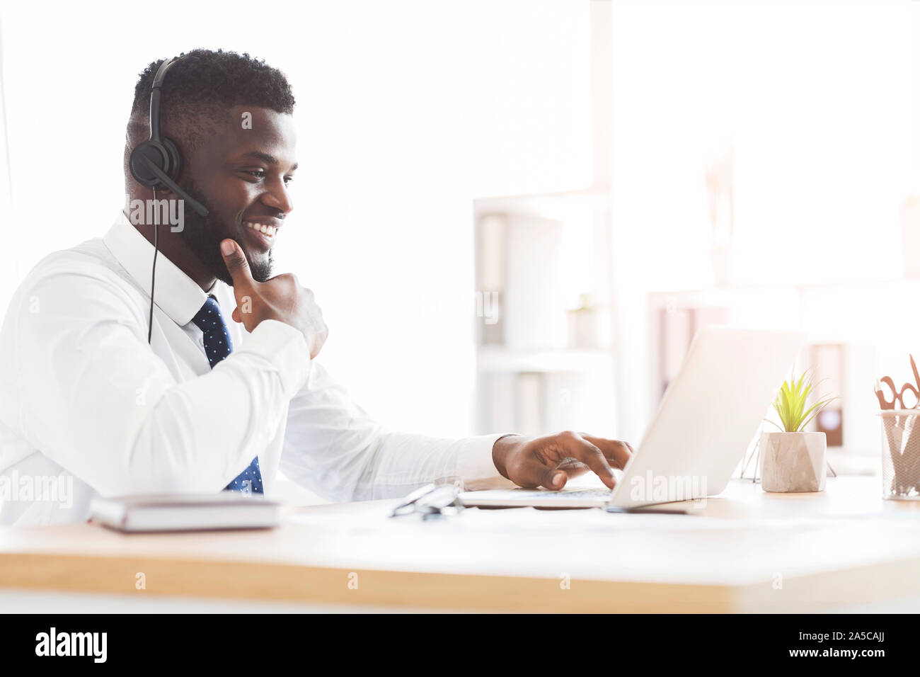 Cheerful employee with headset sitting in front of laptop Stock Photo ...