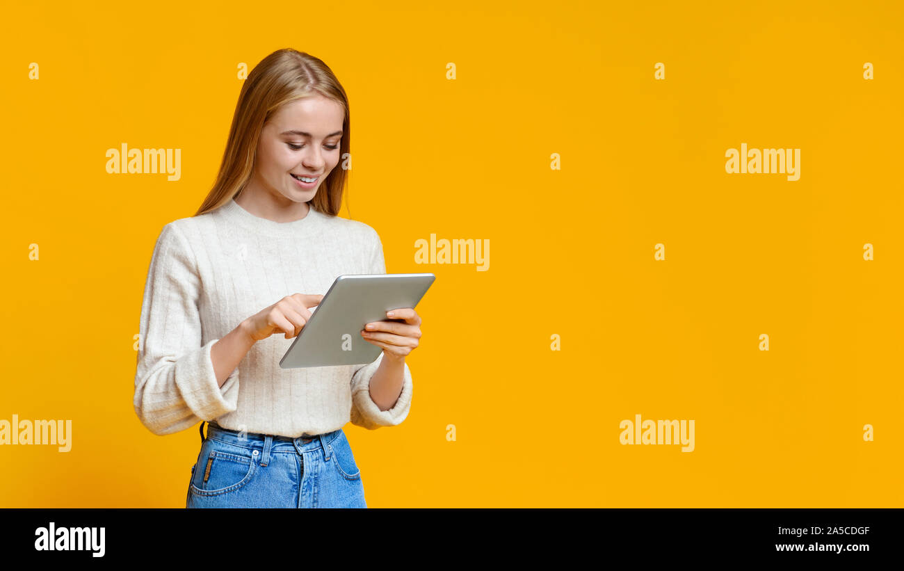 Beautiful teen girl using digital tablet over orange studio background ...