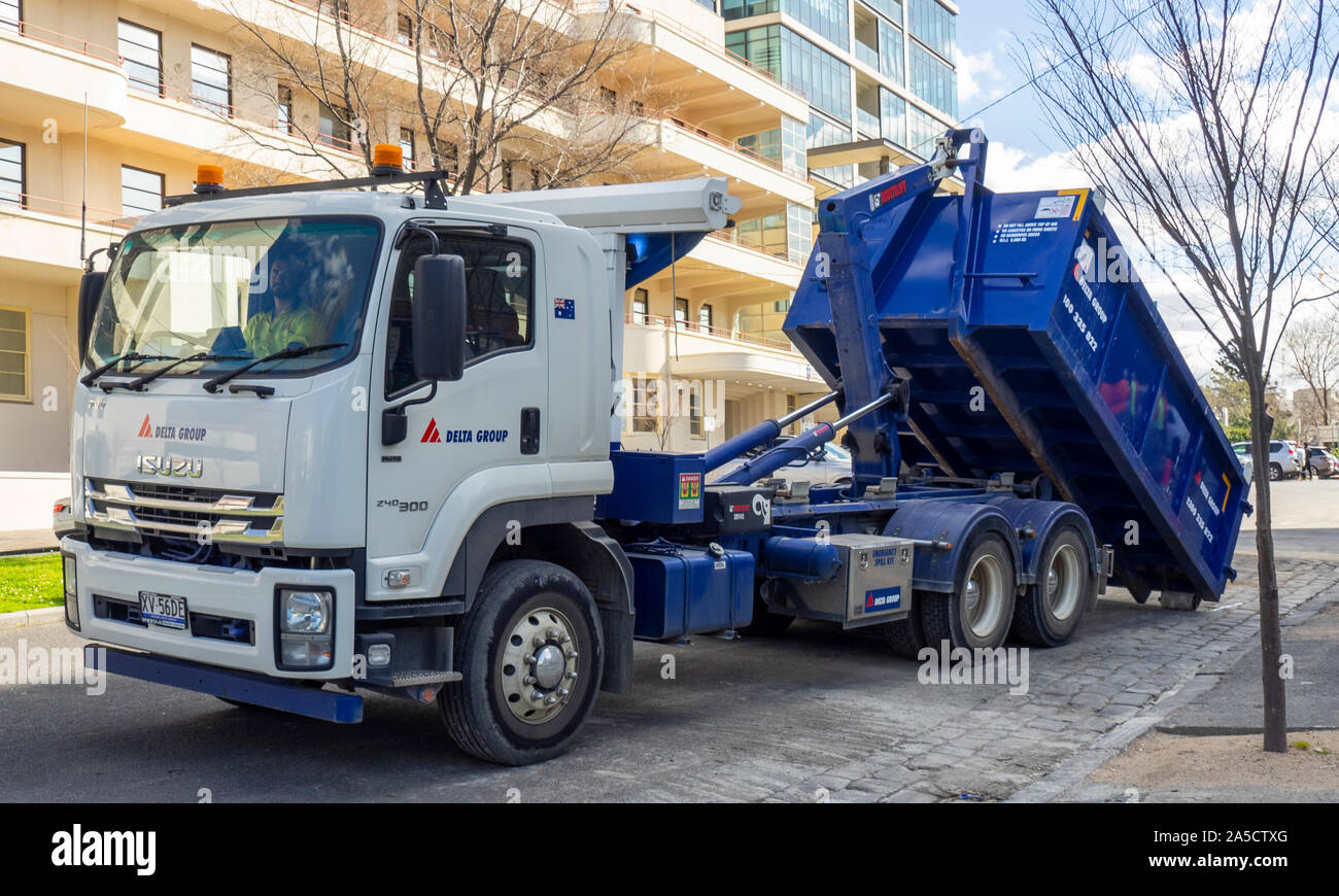 A truck loading a roll-off open to skip bin onto the back of the truck ...