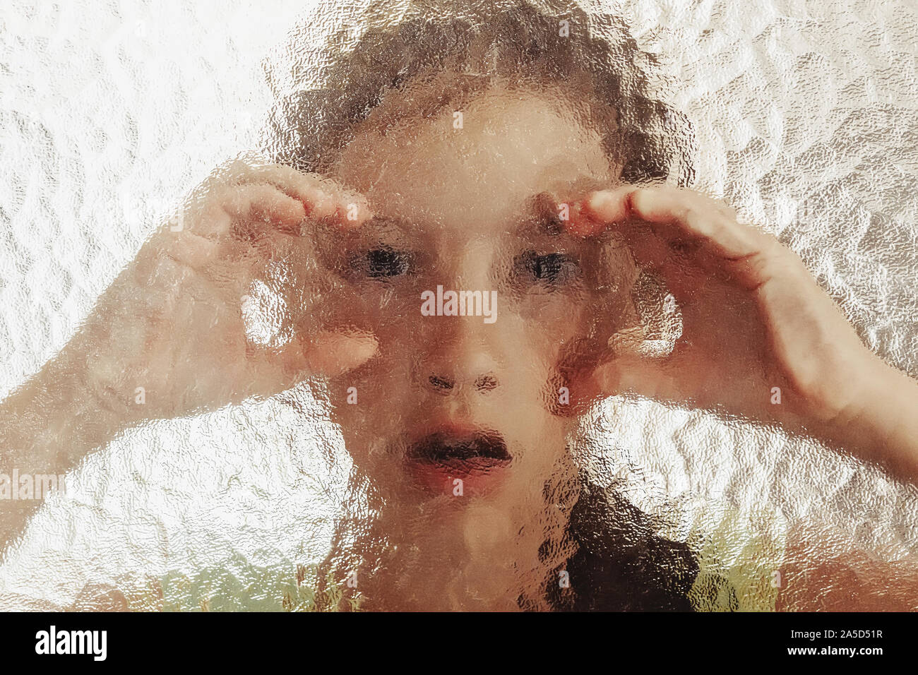 Young scared girl behind glass with her hands on it, fear or horror ...