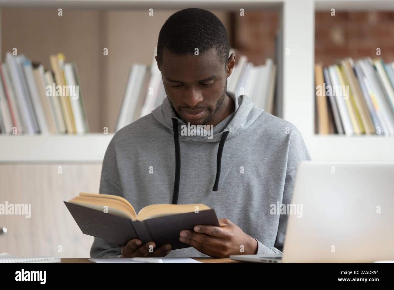 American guy sit at desk in library reading book Stock Photo - Alamy