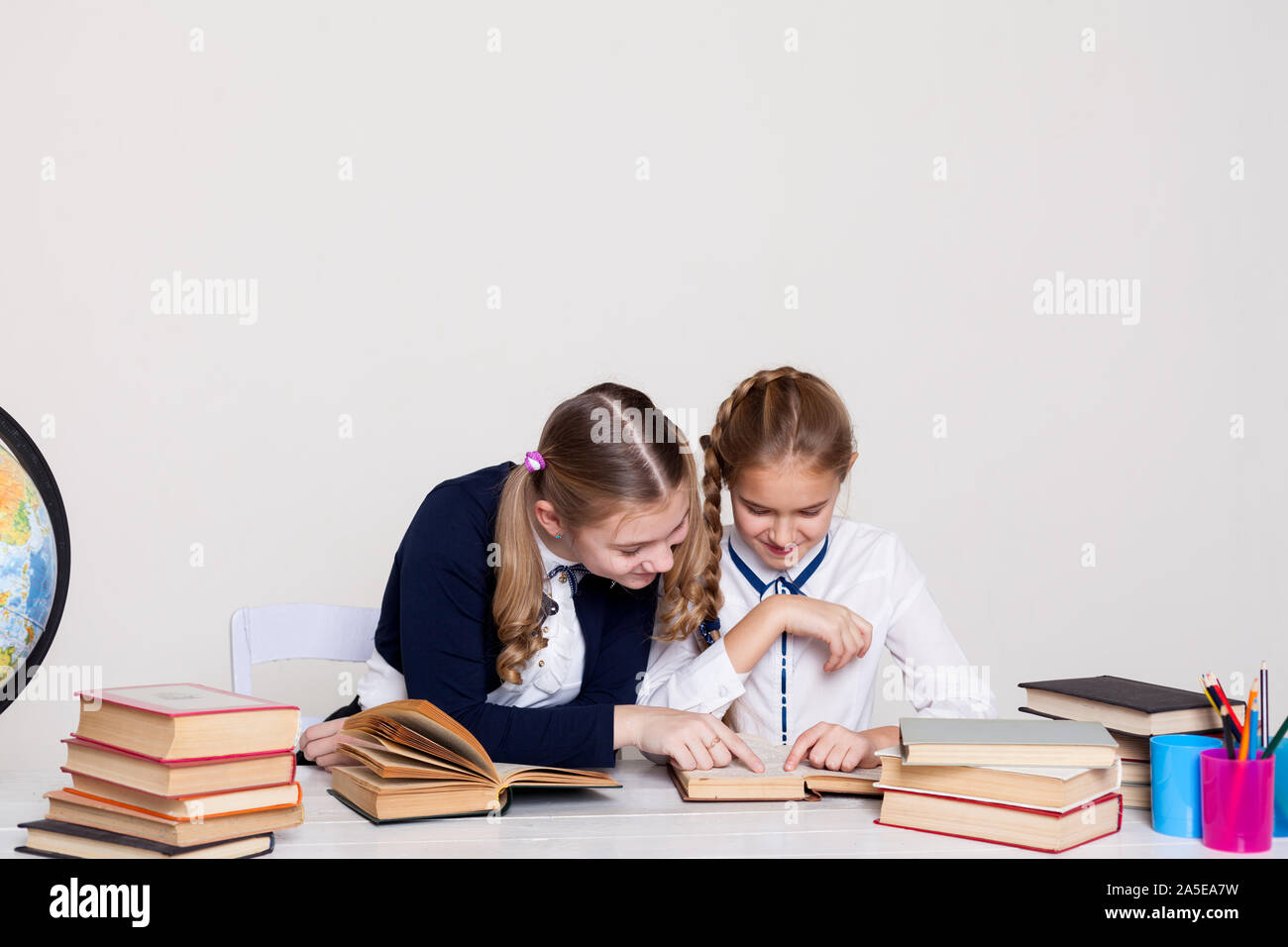 two girls with books and a globe in class at the desk at school Stock ...