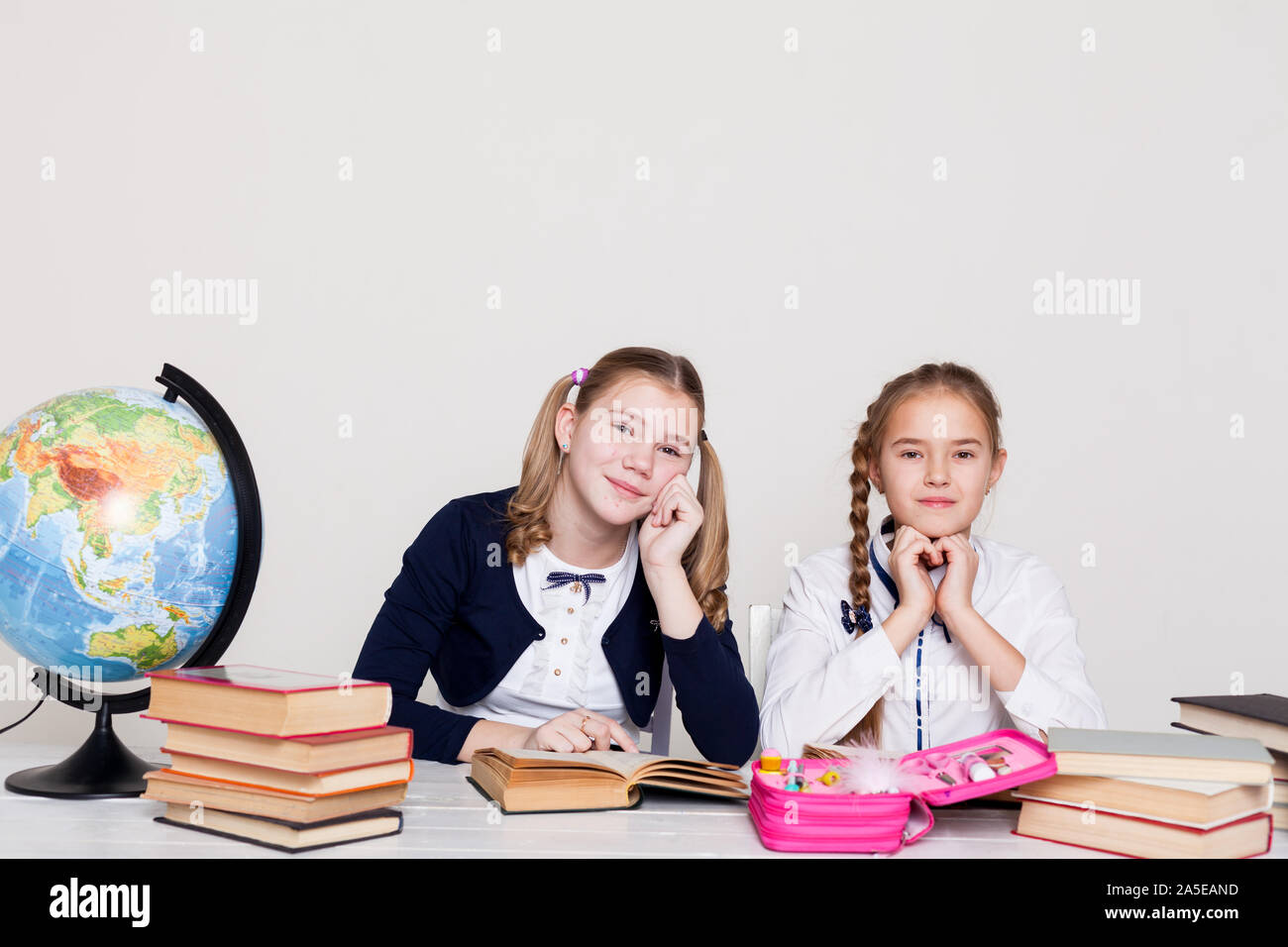 two girls with books and a globe in class at the desk at school Stock ...