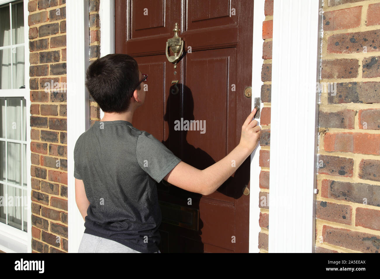 Child ringing doorbell on front door, number 3, wearing glasses, brown ...