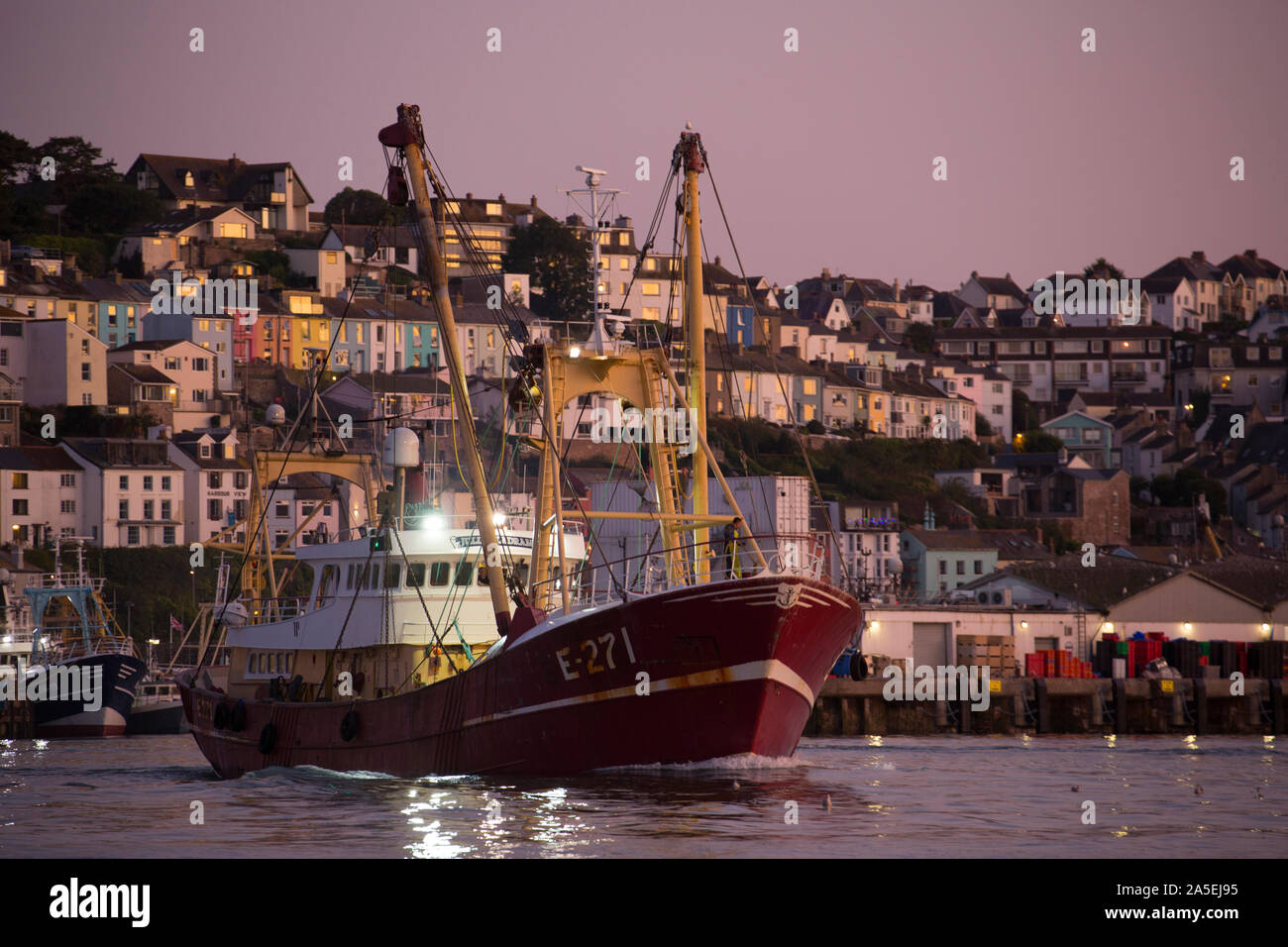 A fishing boat leaving Brixham Harbour in the Autumn as the sun begins ...