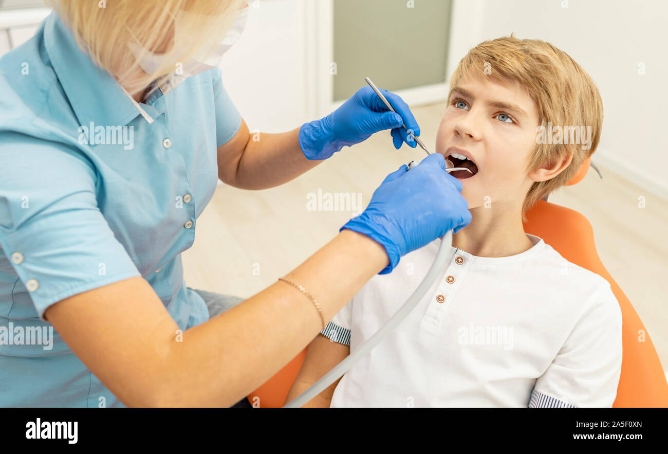 Dentist in blue scrubs using water spray syringe to cleanse young ...