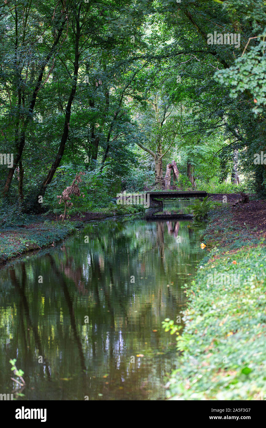 View along ditch with small bridge in park Stock Photo - Alamy