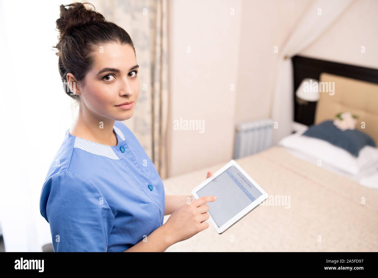 Pretty young chamber maid in uniform holding touchpad while working ...