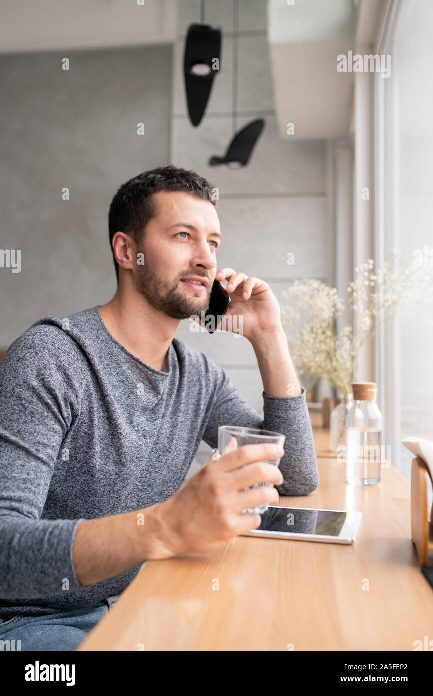 Handsome young man in casual grey pullover talking on smartphone while ...