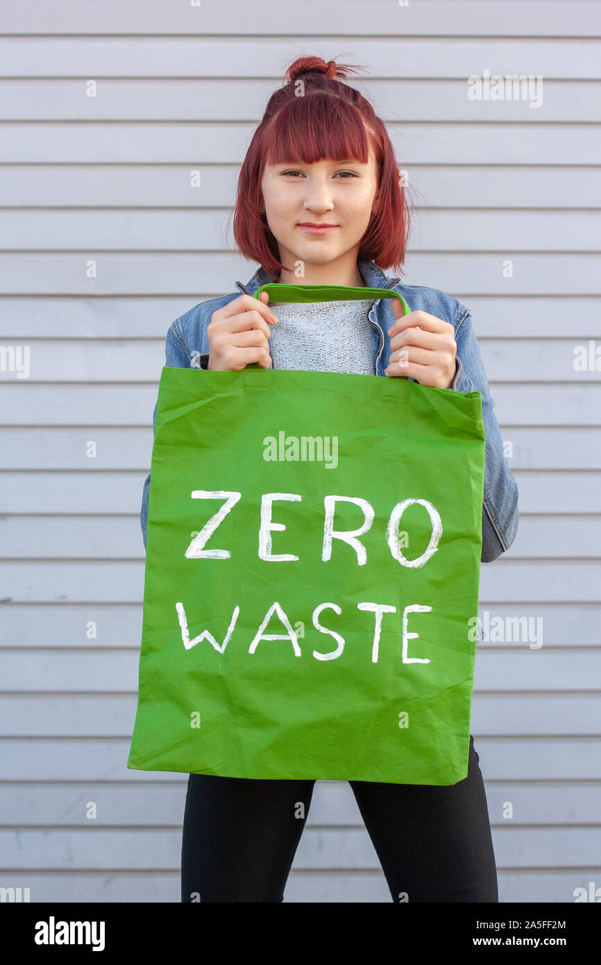 A young smiling girl is holding an empty green eco bag in front of her ...