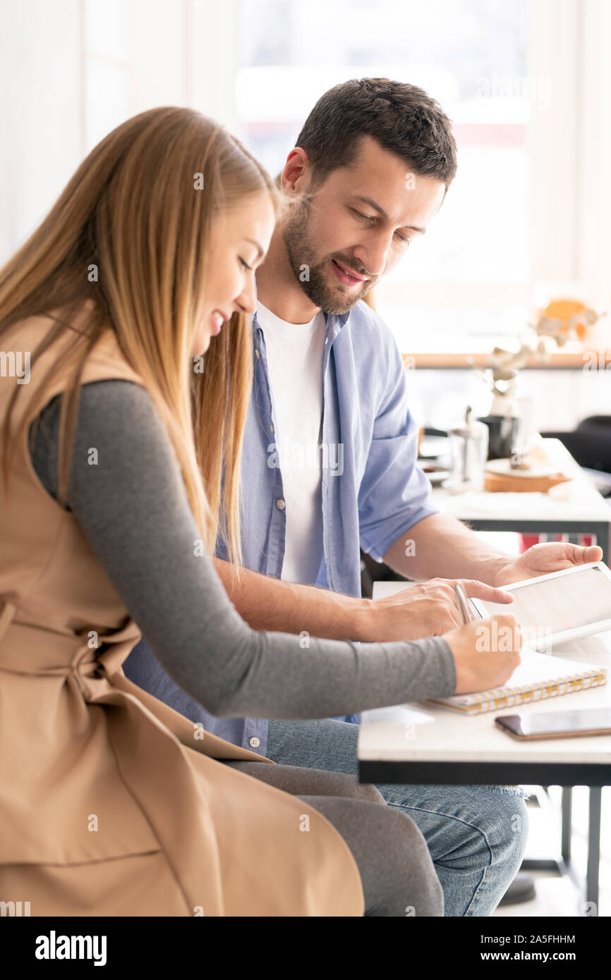 Two young contemporary employees sitting by table in office or cafe ...