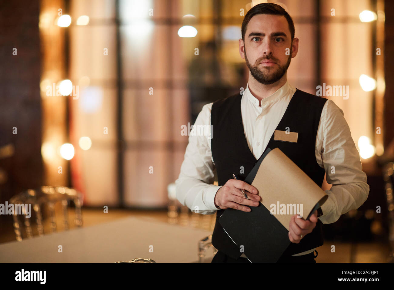 Waist up portrait of handsome waiter looking at camera with serious ...