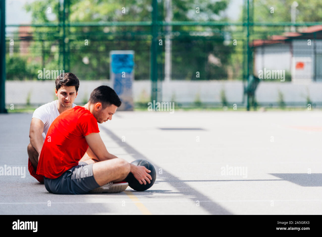 Two strong caucasian athletes resting on the ground at the basketball ...