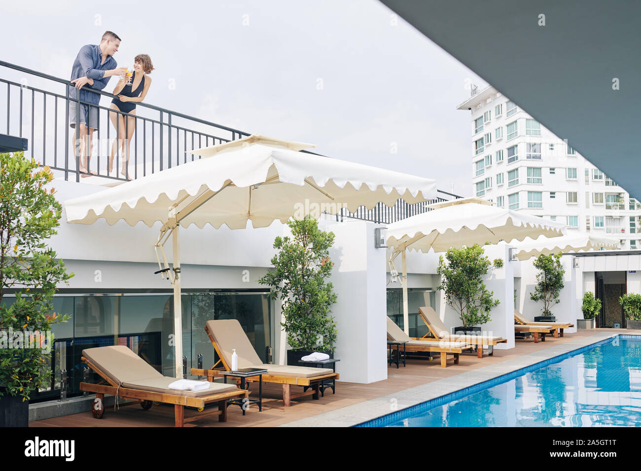 Young flirting couple standing at hotel balcony and drinking juice or ...