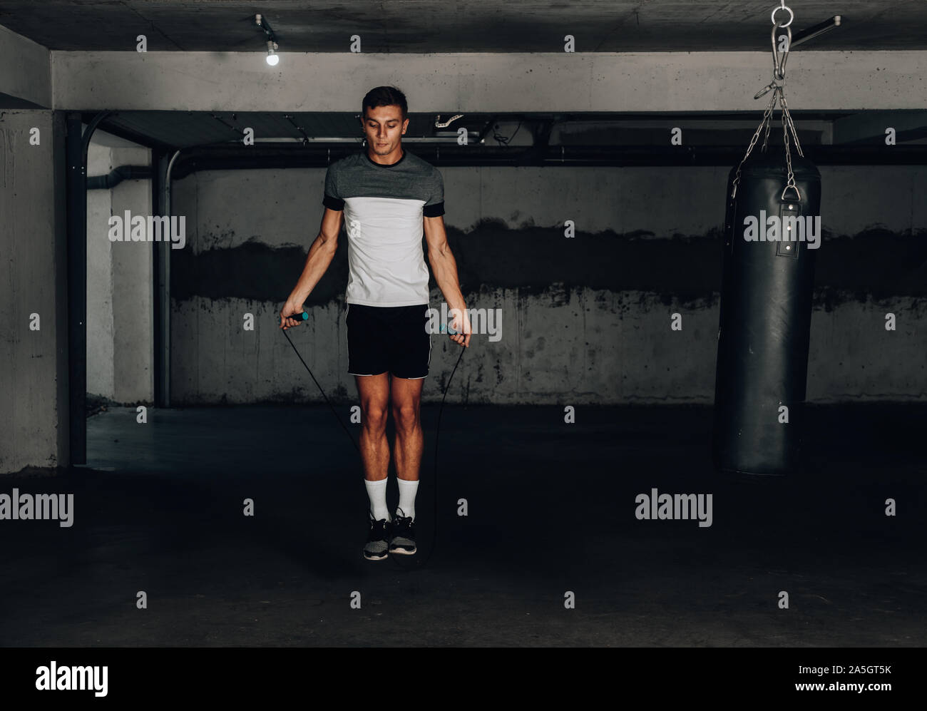Strong muscular man jumping with skipping rope in garage warm up ...
