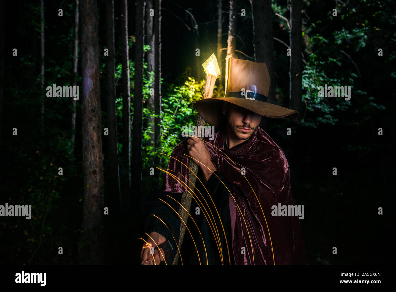 Wizard costume wearing guy with wooden staff standing between trees for ...