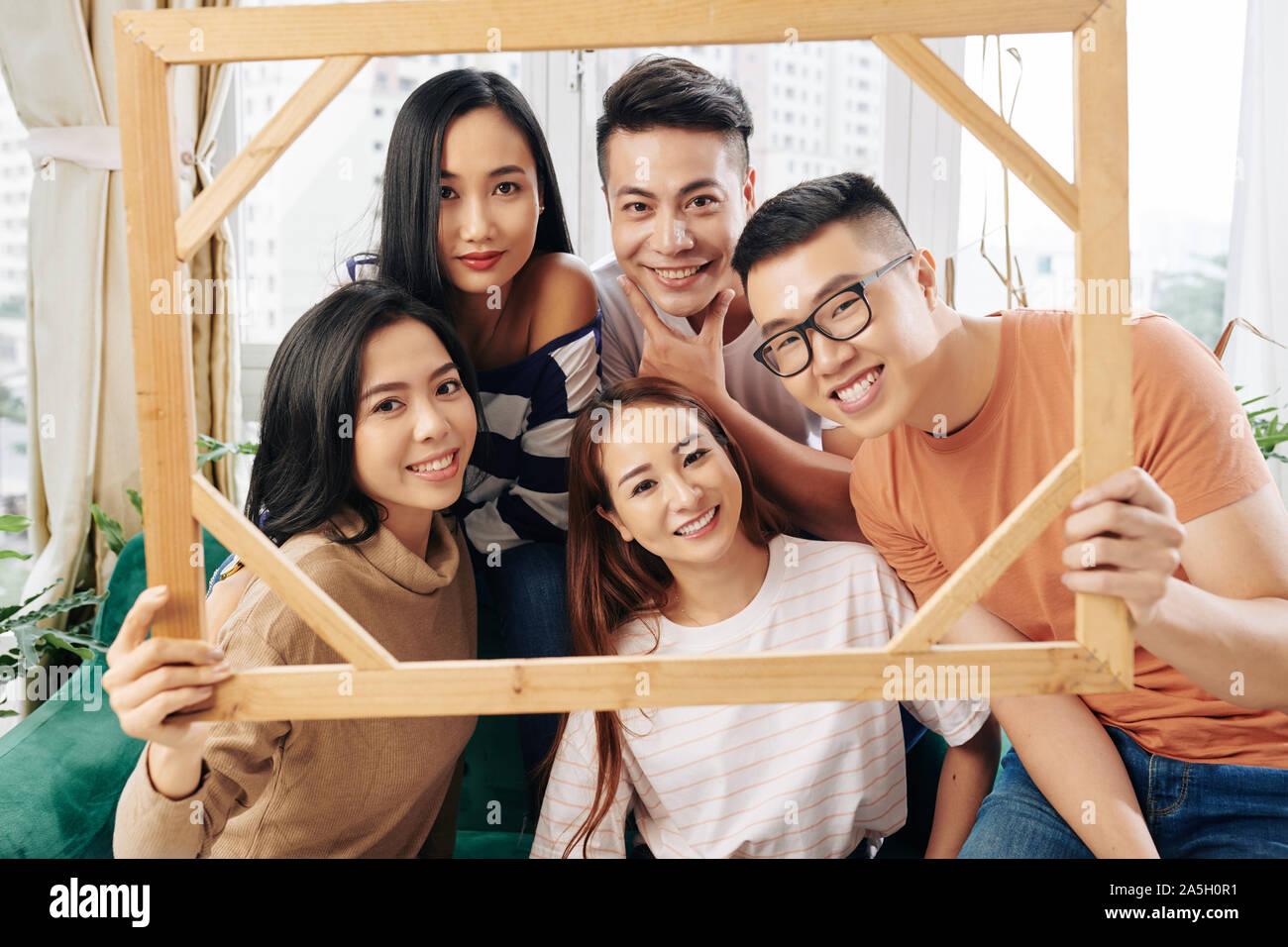 Cheerful beautiful young Vietnamese people holding big wooden frame and ...