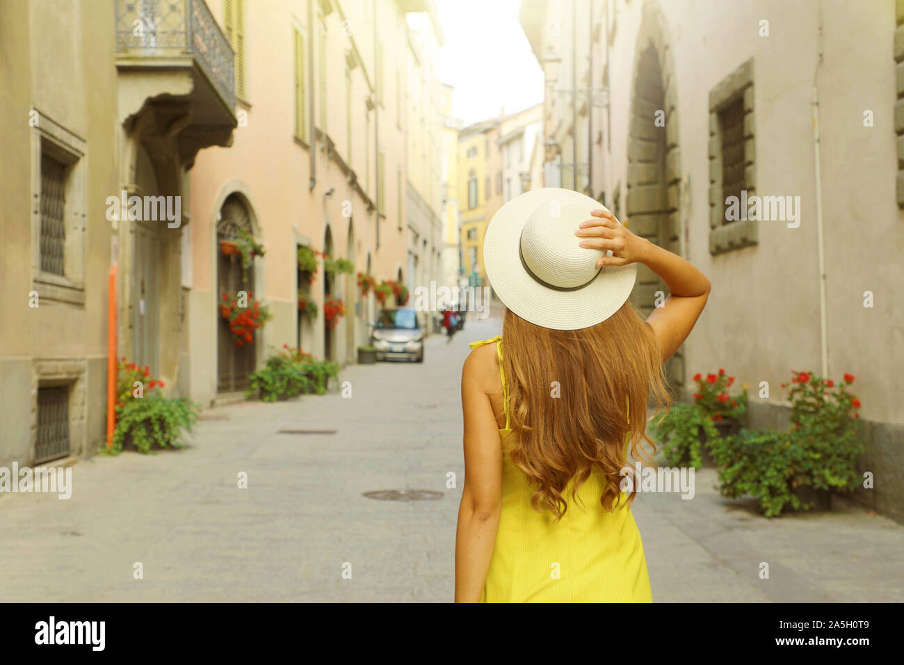 Back view of tourist woman walking and holding hat at Via Pignolo ...