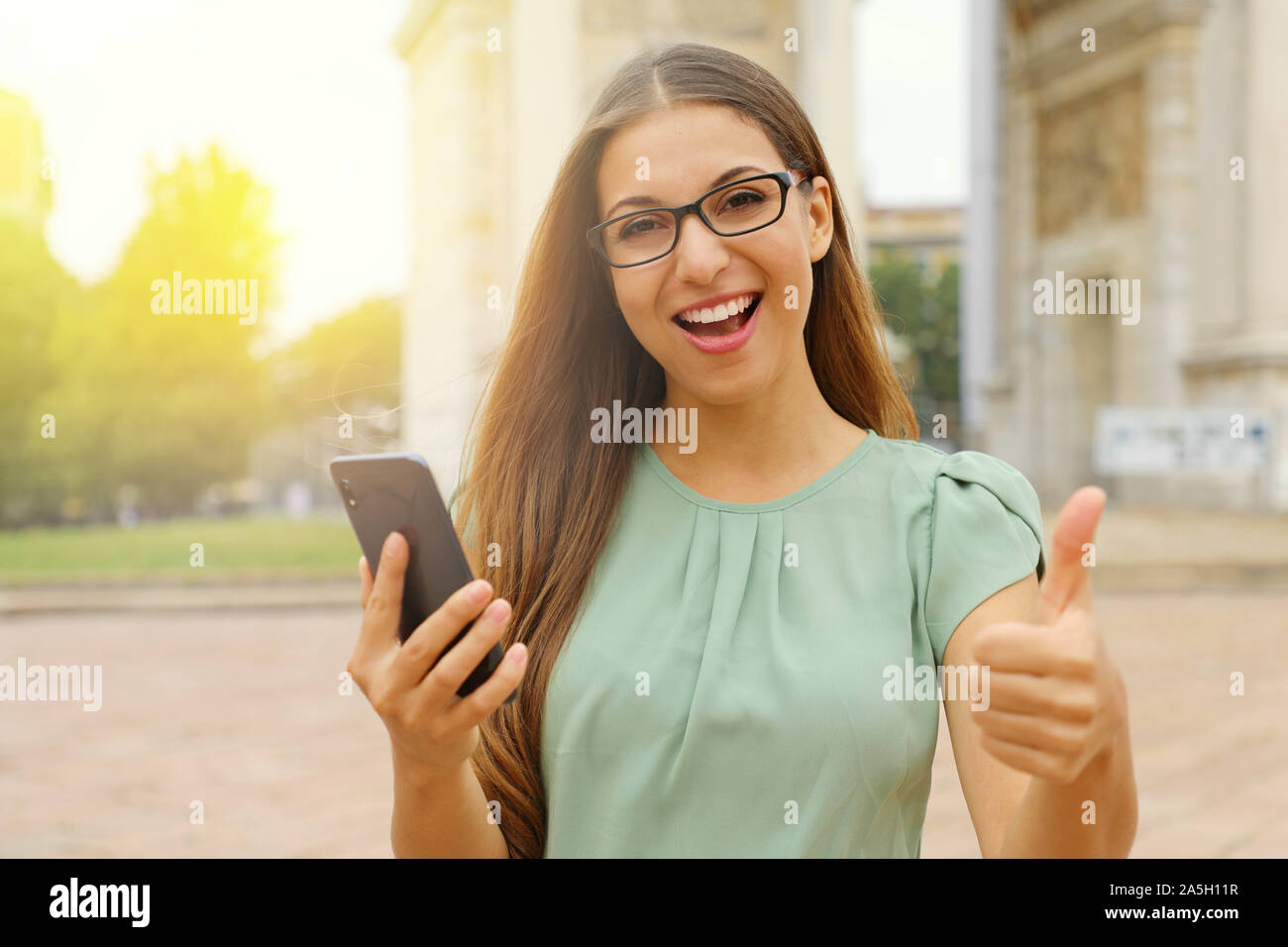 Young beautiful business woman holding smart phone showing thumb up on ...