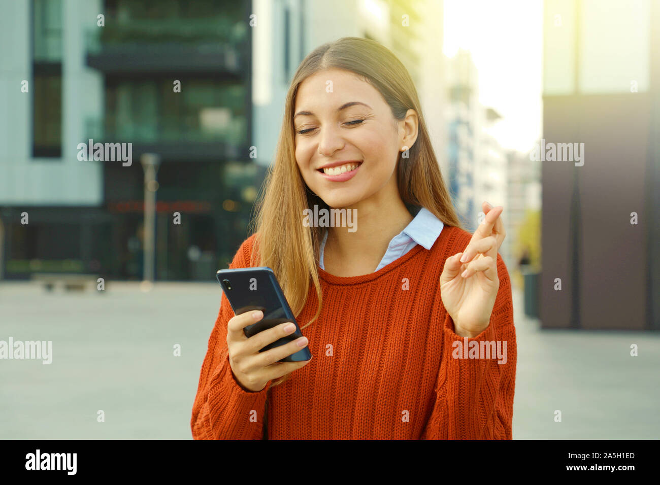 Pretty hopeful girl crossing fingers and bites lip holding a smart ...