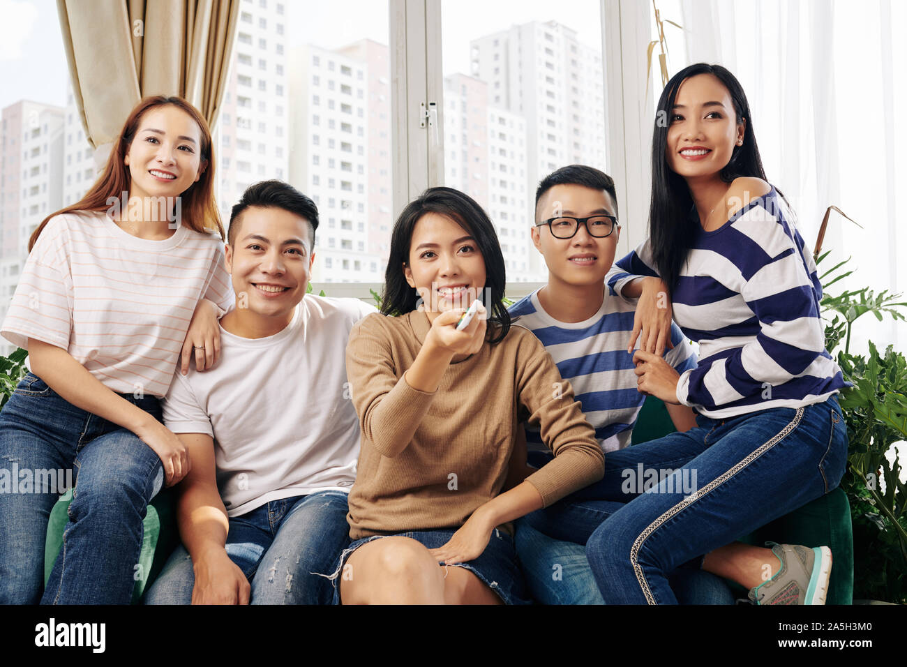 Group of positive friends sitting on sofa and watching tv shows ...