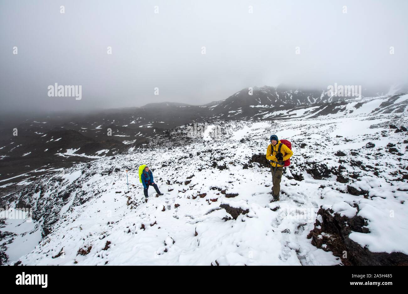 Hikers on hiking trail Tongariro Alpine Crossing in snow over lava ...