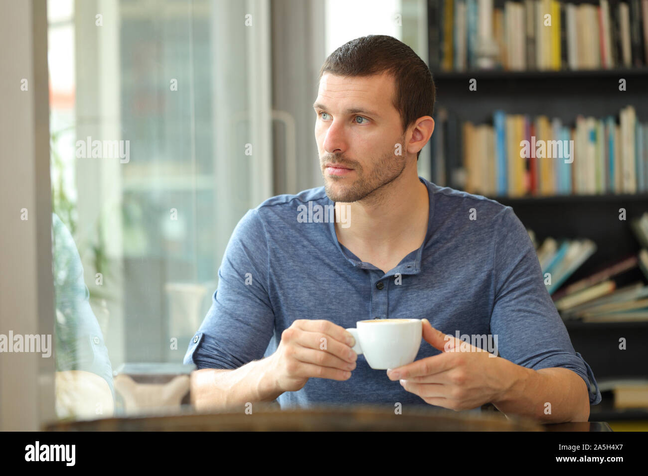 Pensive man holding coffee looking at side through a window sitting in ...