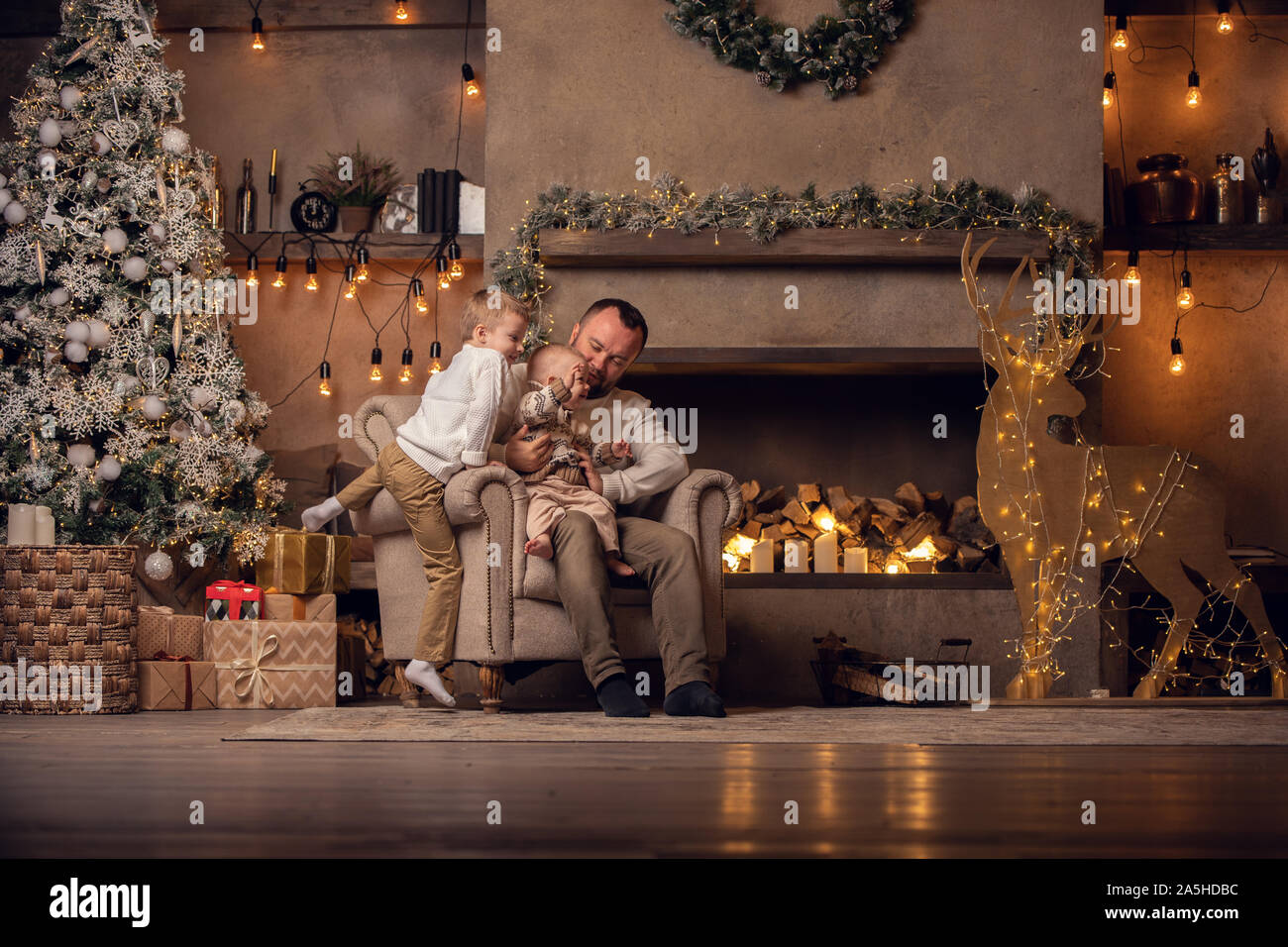 Picture of father with his sons sitting in armchair by New Year tree ...