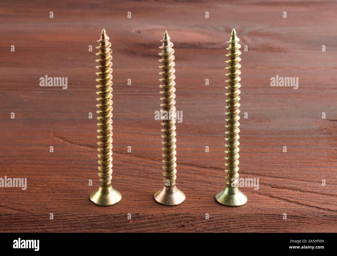 Three long metal screws on a brown wooden background Stock Photo - Alamy