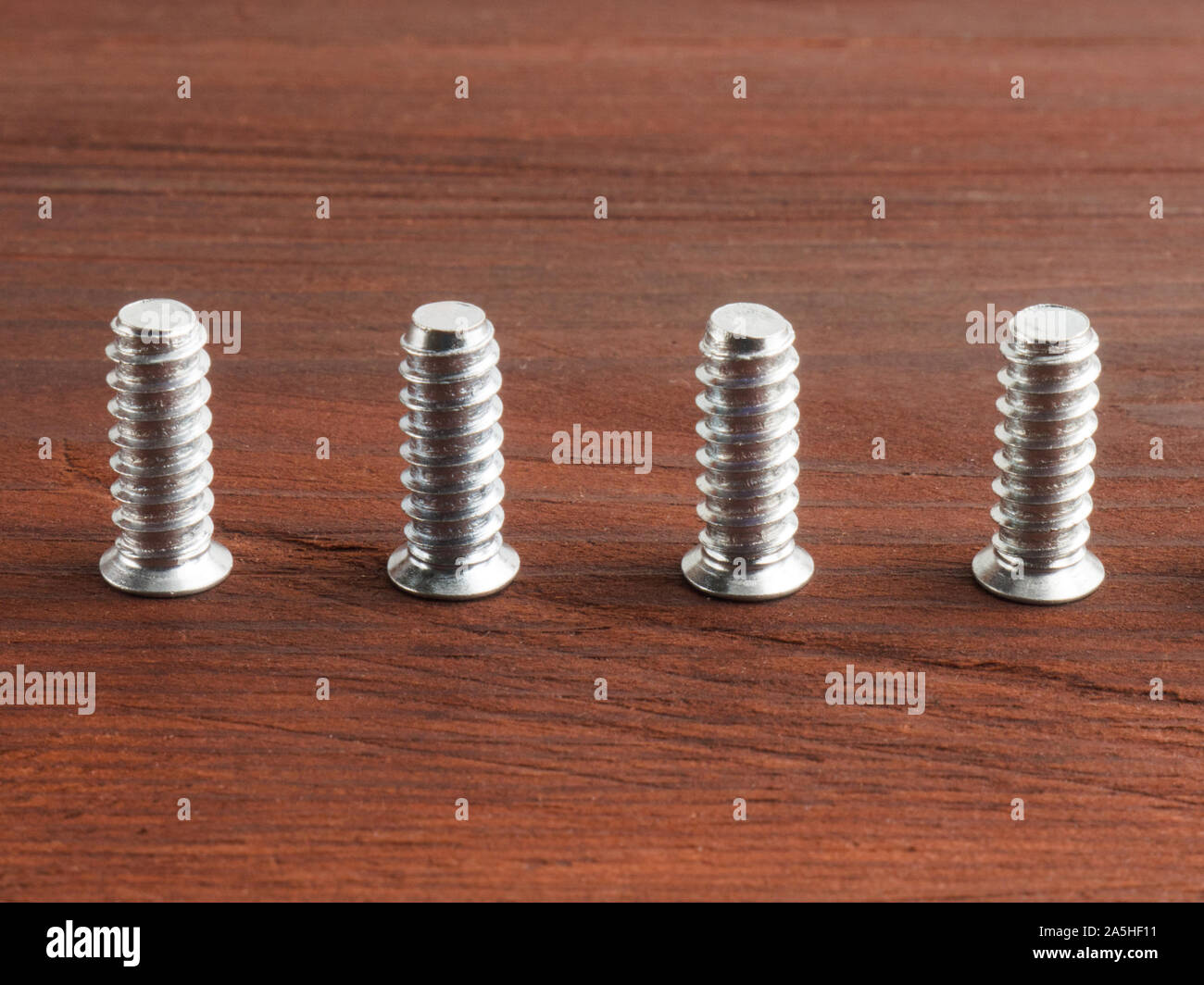 Set of four silver color steel screws on a brown wooden background ...