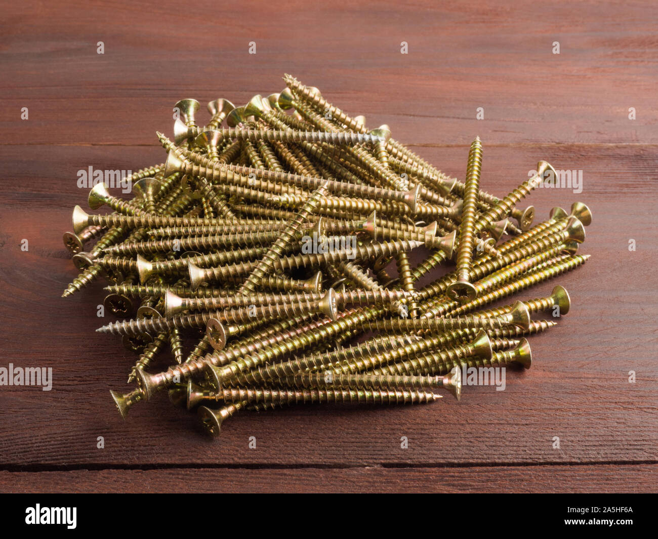 Set of long metal screws on a brown wooden background. Industrial ...