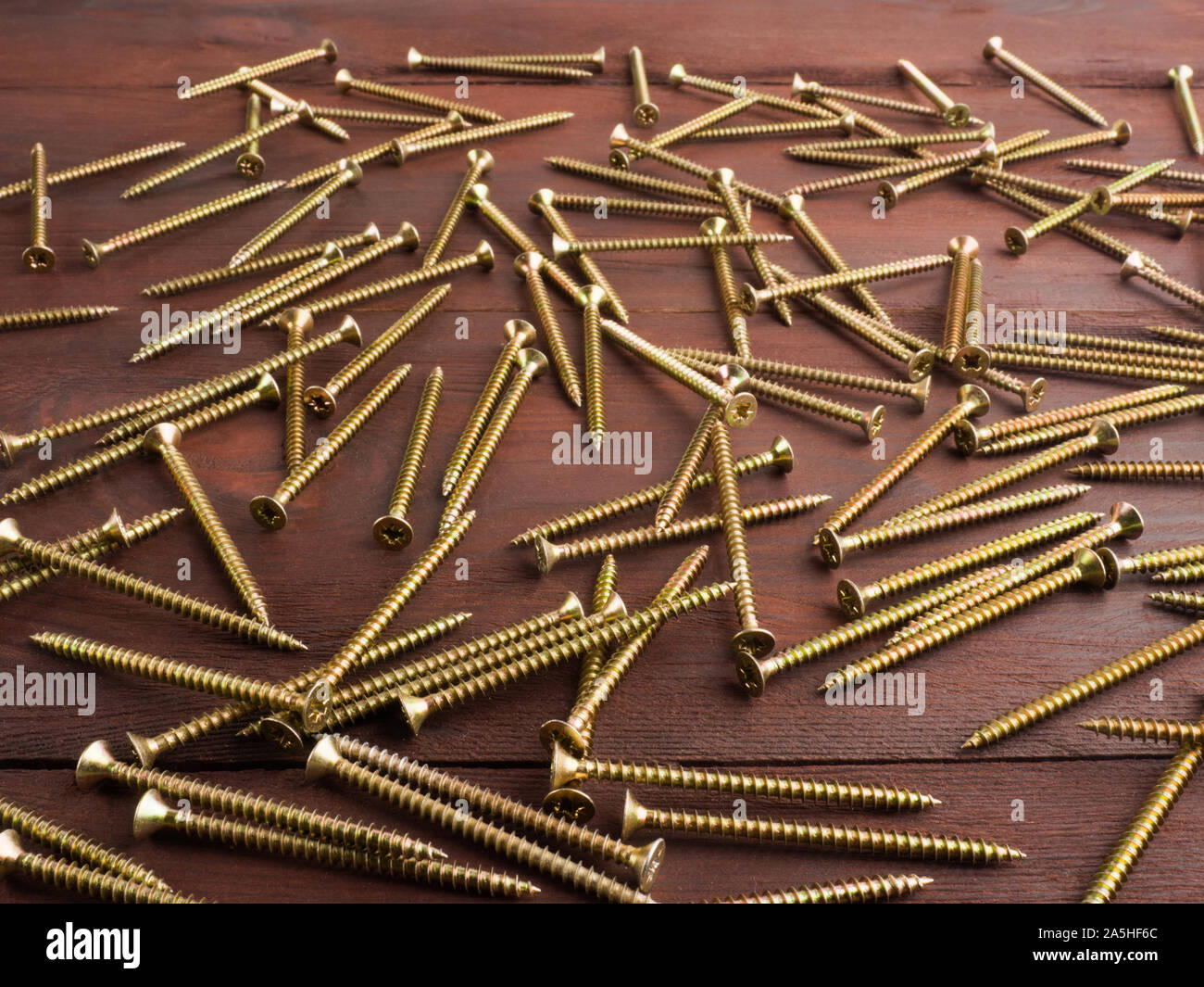 Set of long metal screws on a brown wooden background. Industrial ...