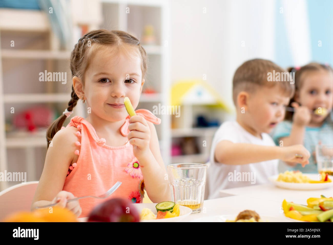 Cute child girl eats healthy food with kids group in kindergarten Stock ...