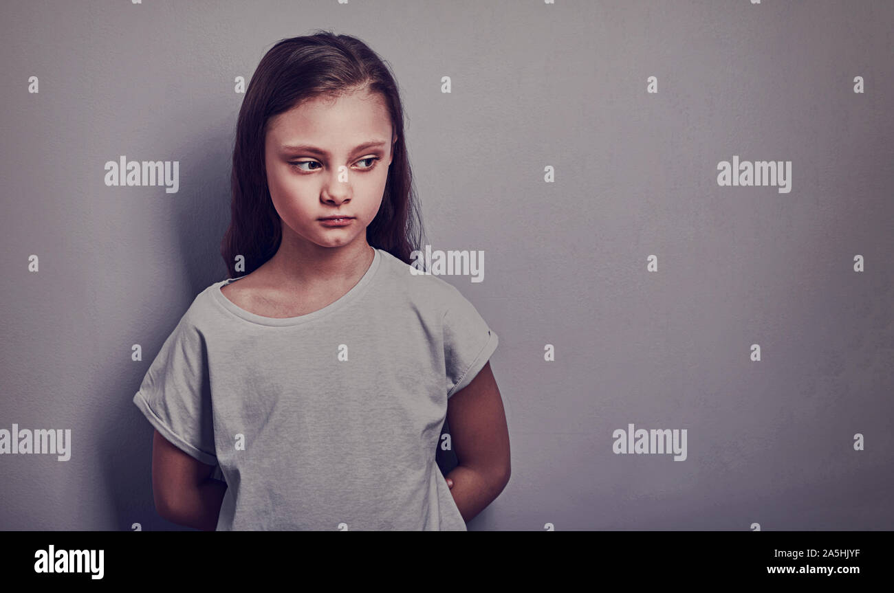 Offended, punished kid girl with serious emotions looking on dark wall ...