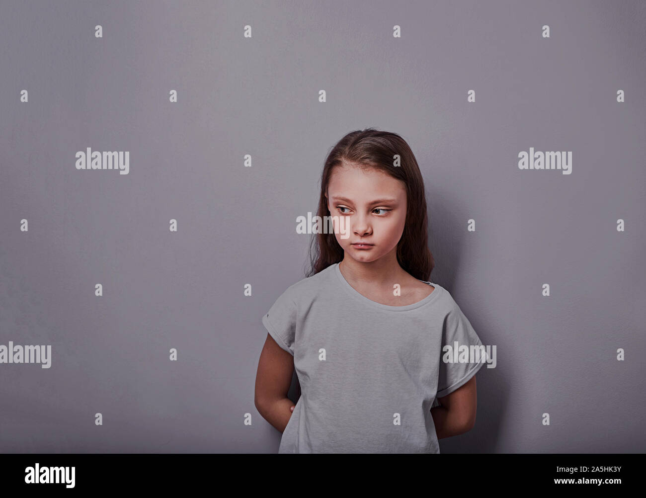 Offended, punished kid girl with serious emotions looking on dark wall ...