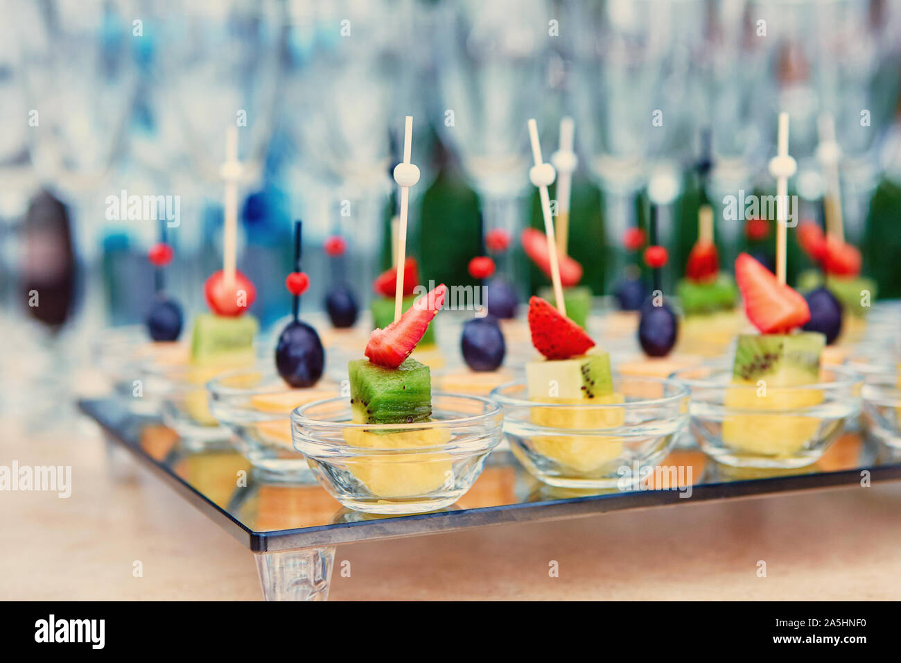 Fruit canapes on a glass tray, on the background of wine glasses and ...
