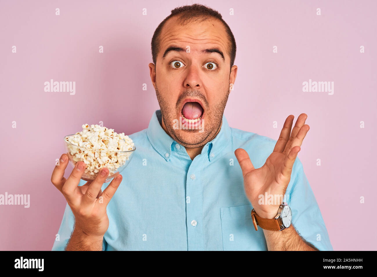 Young man holding bowl with popcorn standing over isolated pink ...