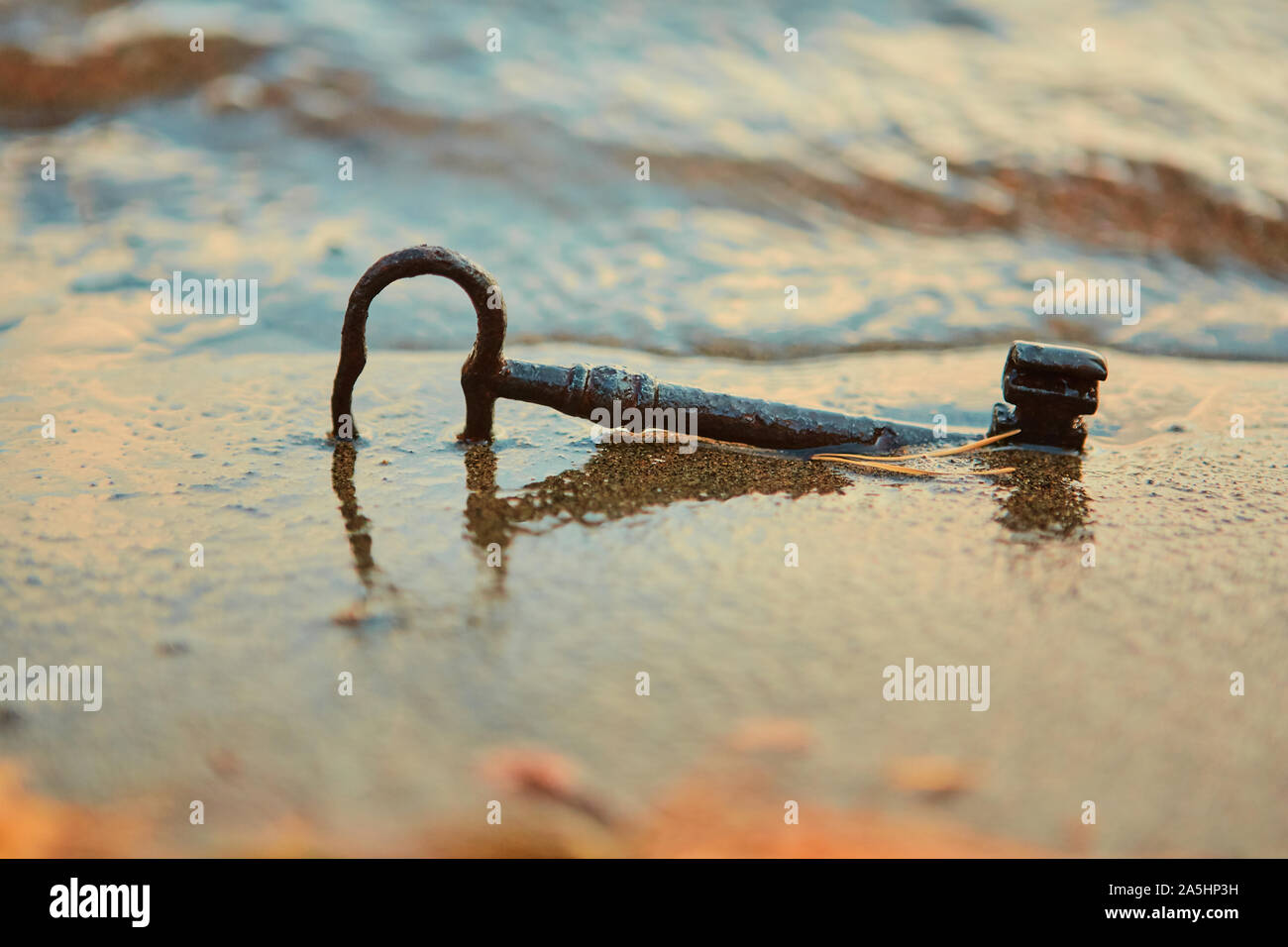 An old rusty lost treasure key, lying in the sand in the surf on the ...