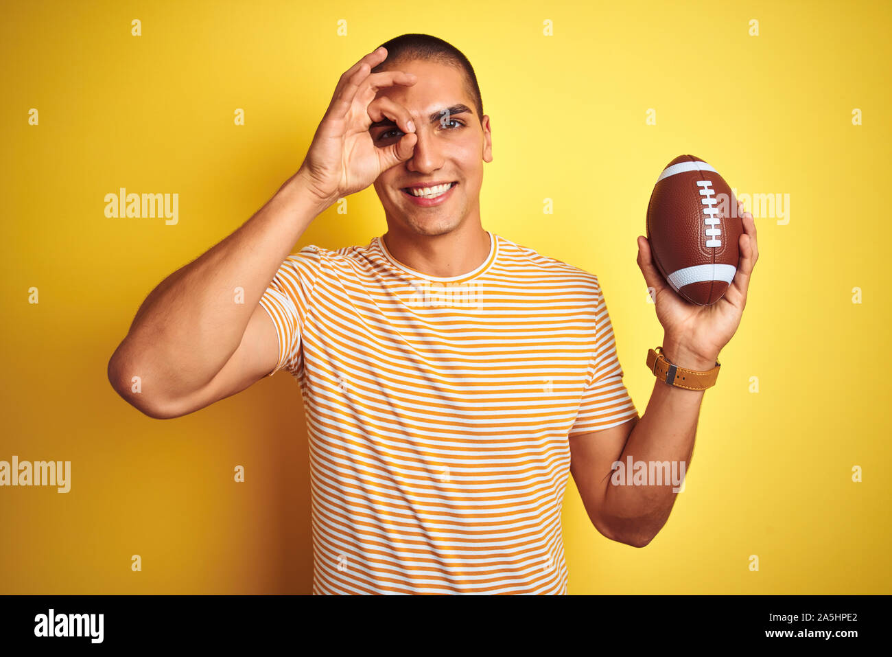 Young rugby player man holding a football ball over yellow isolated ...