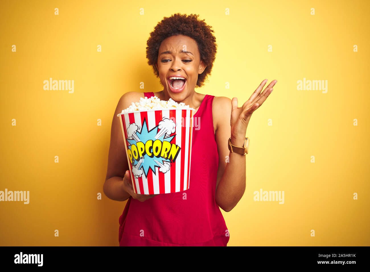 African american woman holding pack of popcorn over yellow isolated ...